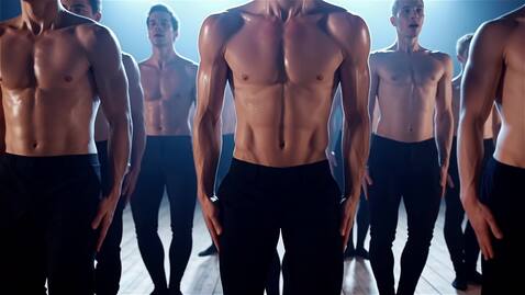 A formation of shirtless male dancers stands in